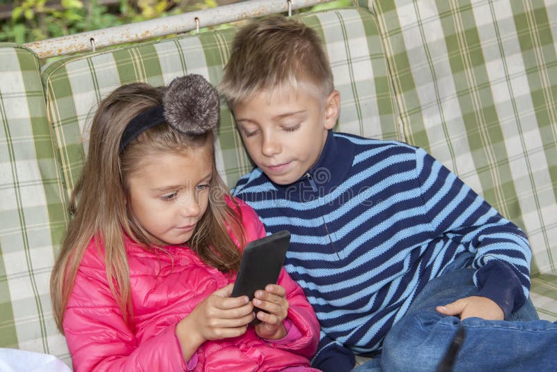 Girl Is Sitting On Swing And Playing Mobile Games On Smart Phone Boy Sits Next To Her And 4893