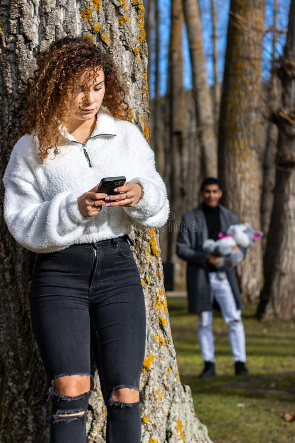 Girl Texting Behind a Tree while Boyfriend Approaches Her with a Teddy ...