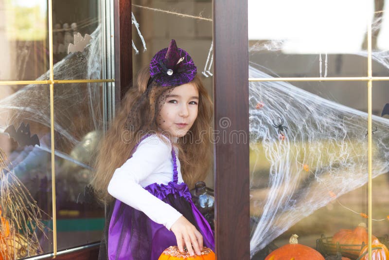A Girl in a Witch Costume on the Windowsill by the Window is Playing ...