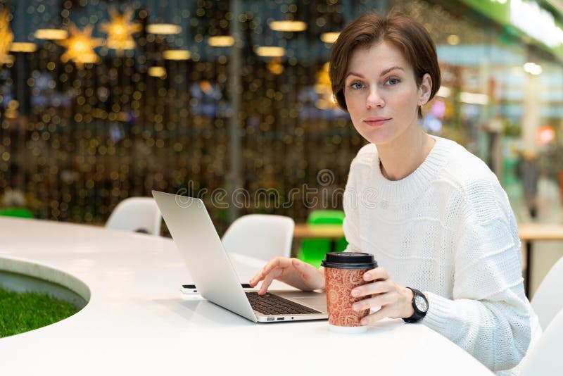 Girl Works on a Laptop and Drinks Coffee with a Smile Looking at the ...