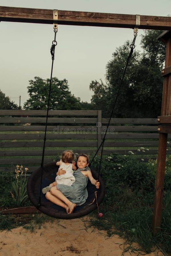 Girls - Sisters Ride on a Swing in the Evening in the Yard Stock Photo ...