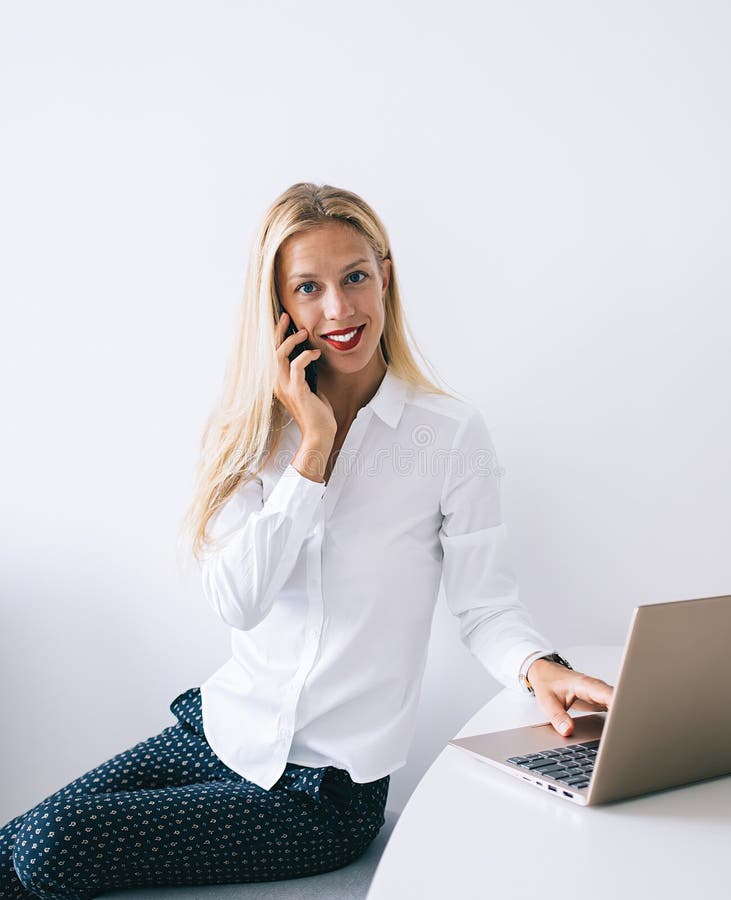 Glad Female Sitting at Table Talking on Mobile and Typing on Laptop ...