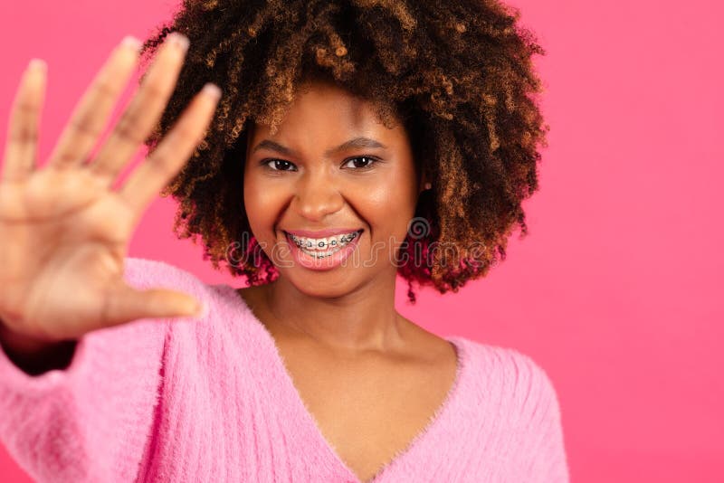 Glad Young Black Curly Female In Casual With Braces Waving Hand At