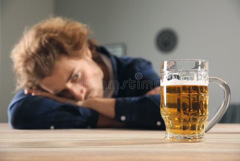 Glass of Beer and Drunk Young Man at Table. Alcoholism Concept Stock ...
