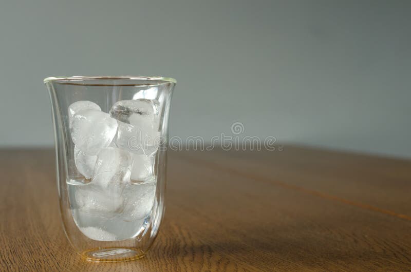 Glass with Half Melting Ice Pieces on the Wooden Table. Ice is ...