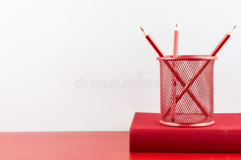 A Glass with Three Red Pencils Stands on a Red Book on a Red and White ...