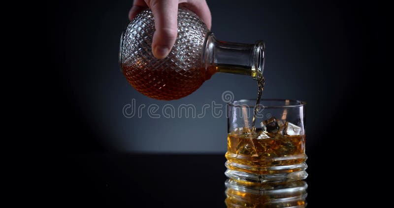 Glass of Whiskey with Ice Cube. Alcohol Pouring in the Glass from the ... Glass of Whiskey with Ice Cube. Alcohol Pouring in the Glass from the ...