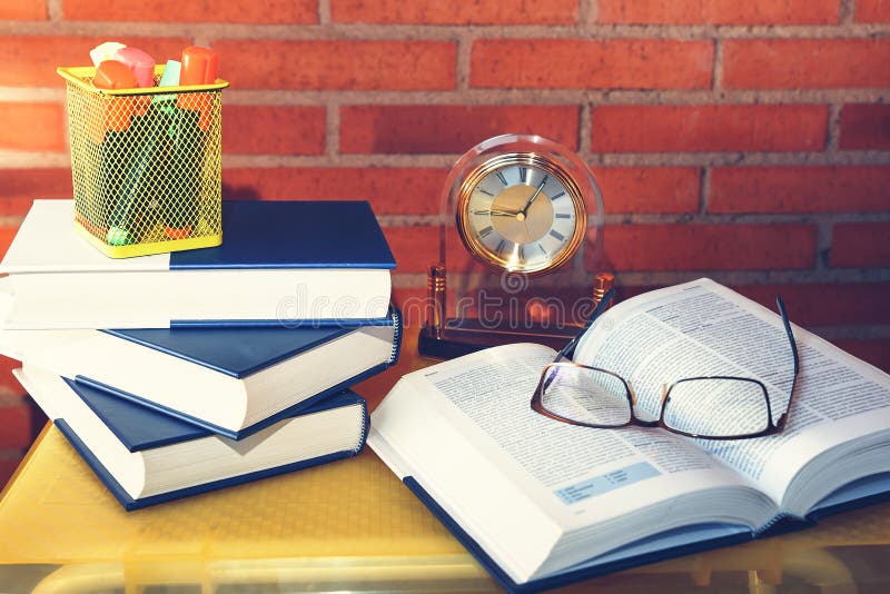 Glasses on an Open Book on a Yellow Table with a Clock and Other Books ...