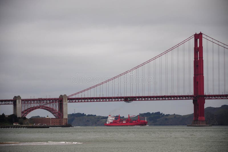 Golden Gate Bridge with Red Ship Passing Underneath on a Cloudy Day ...