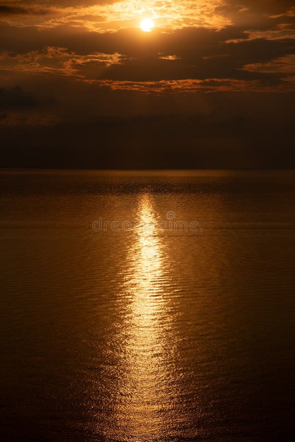 Golden Sunset Reflecting on Calm Ocean Water with Dramatic Clouds Stock ...