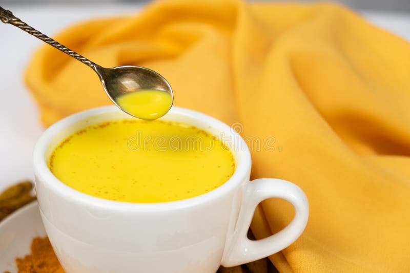 Golden Milk with Turmeric in a Cup, Stirring the Drink with a Spoon ...