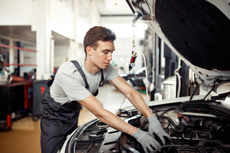 A Good-loking Young Mechanic is Reparing a Vehicle at His Work Stock ...