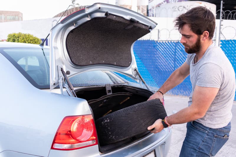 Young Man Taking the Spare Tire Out of the Trunk of a Car, on the Road ...