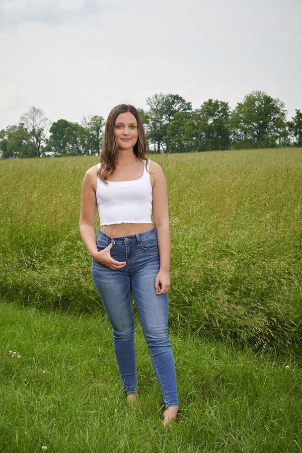 Gorgeous Young Woman In Blue Jeans And White Tank Top Poses Outside