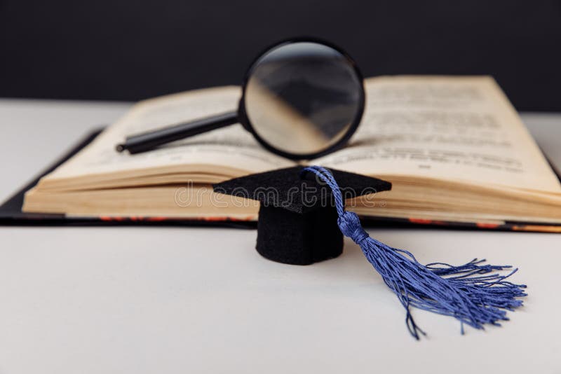 Graduation Cap and Magnifier on Open Book on White Table. Education ...