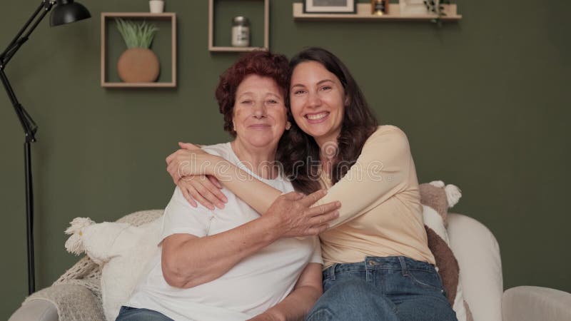 Grandmother And Granddaughter Are Hugging While Sitting On The Sofa In