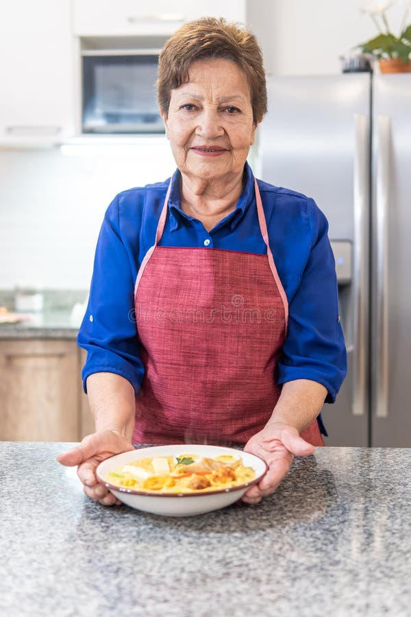 Granny Looking at Camera Offering a Soup Plate in the Kitchen Stock ...