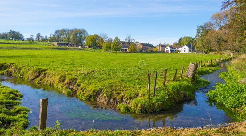 Grassy Green Edge Of A Stream Through A Small Village In Bright Sunlight At Fall Voeren