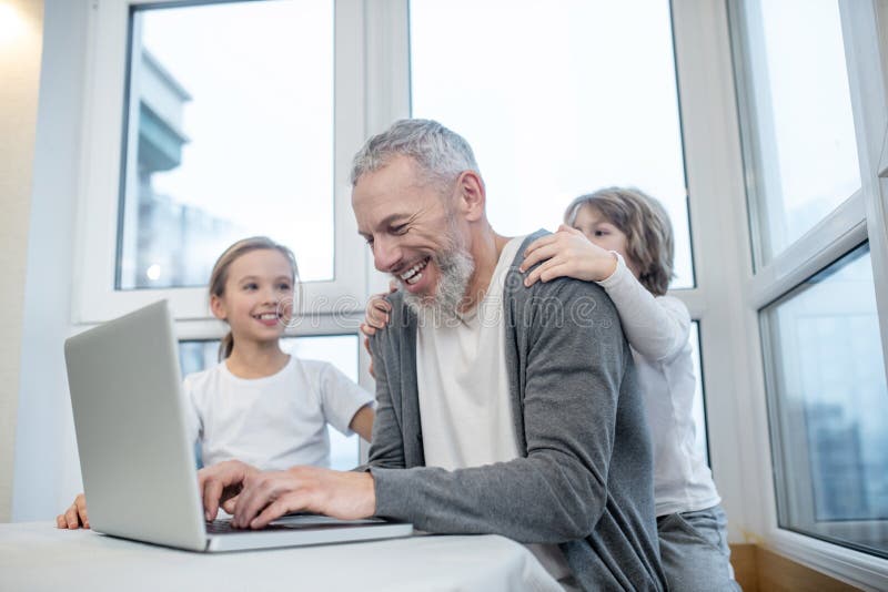 Gray-haired Bearded Man Working on Laptop while His Kids Interfering ...