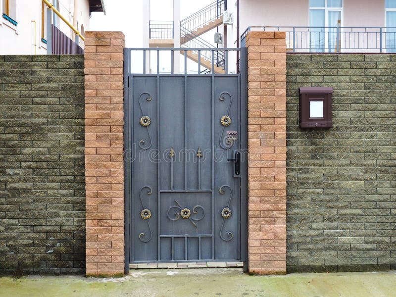 A Gray Iron Gate with a Forged Pattern in a Fence with Decorative Brick ...