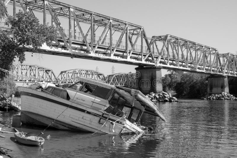 Grayscale of a Discarded and Destroyed Boat with a Bridge in the ...