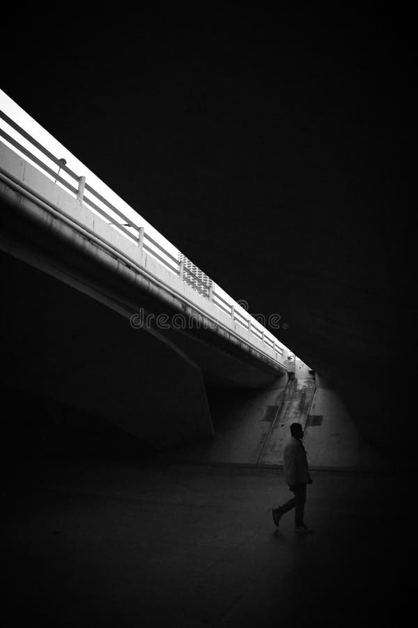 Grayscale of a Man Walking on a Pedestrian Walkway Under a Bridge Stock ...