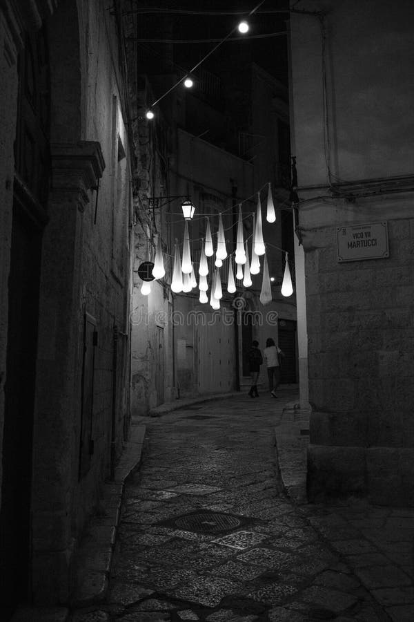 Grayscale Vertical Shot of a Narrow Stone Ally at Night with Hanging ...