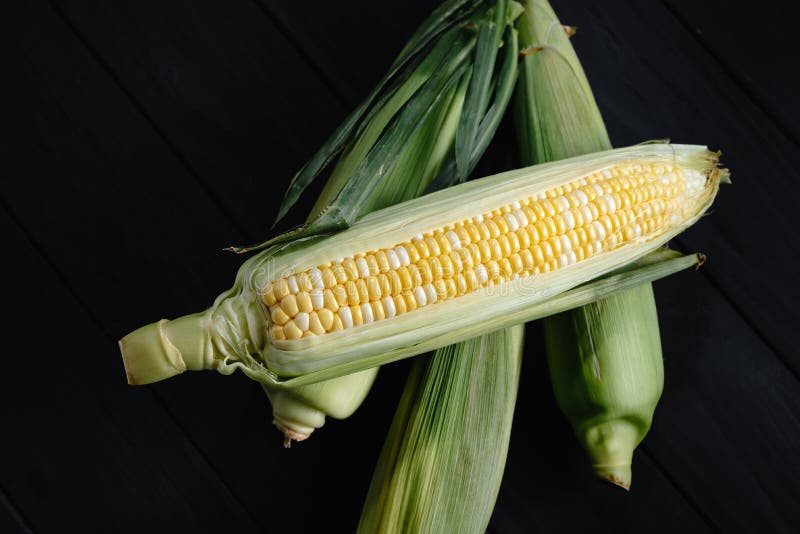 Green Corn on a Dark Background. Corn Cobs in Leaves on a Wooden ...