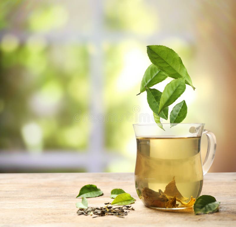 Green Leaves Falling into Cup of Tea on Table Against Background. Space ...