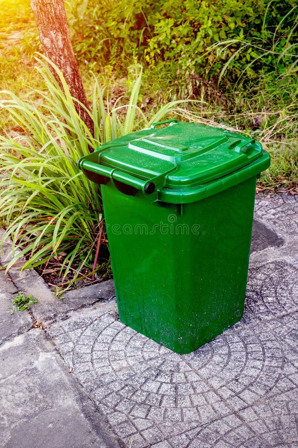 Green Outdoor Trash Bin on Pavement Near Plants and Trees Stock Photo ...