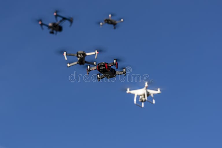 A Group of Multiple Drones Fly Together through the Air Against a Blue ...