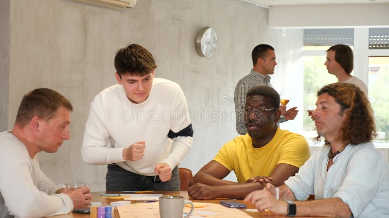 Excited Man Standing on Foot Playing Board Game with Interested Guys ...