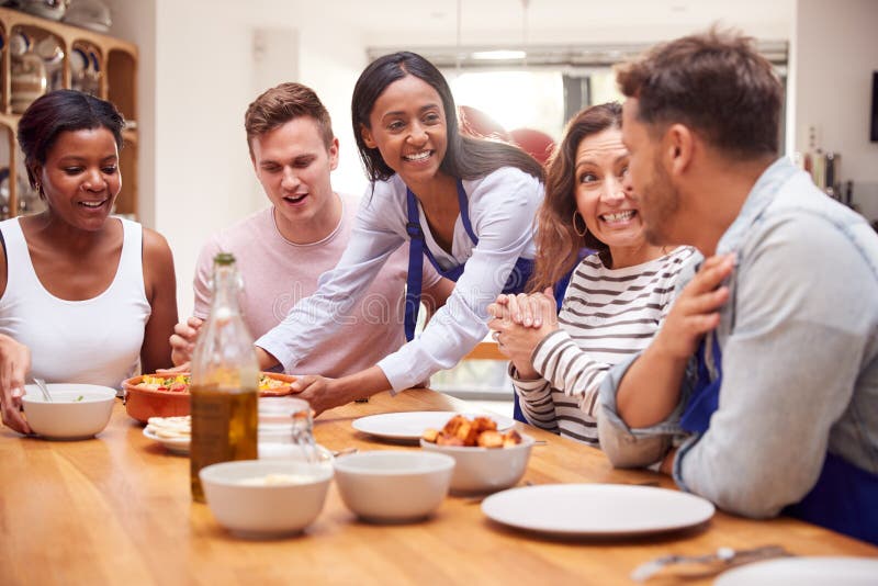 Group of Friends Sitting Around Table Eating Meal at Home Together ...