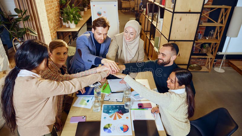 Group of Multicultural Colleagues Join Hands in Team Huddle Around Desk ...
