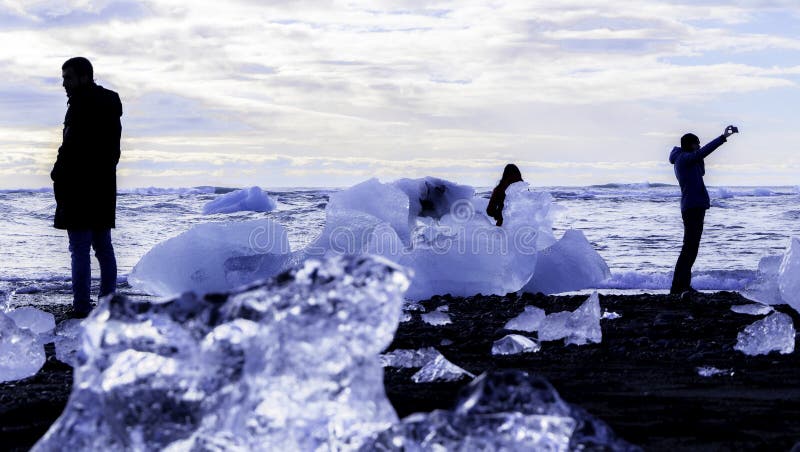 A Group of People are Standing on a Beach with a Large Amount of Ice ...