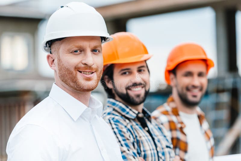 Group of Smiling Architects in Hard Hats Looking Stock Photo - Image of ...