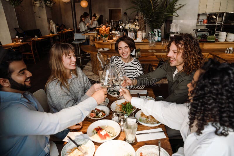 Group of Smiling Friends Clinking Wine Glasses while Dining in ...
