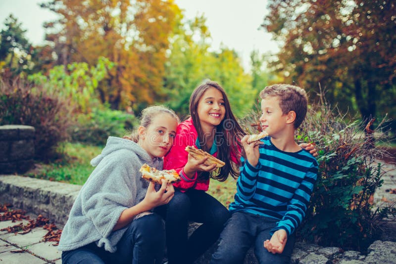 Group of a Three Children Laughing, Talking and Eating Pizza Outdoors ...
