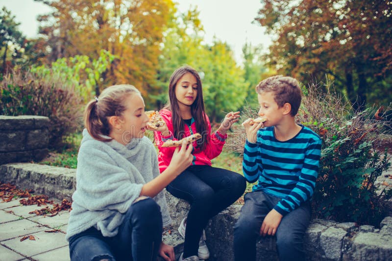 Group of a Three Smiling Children, Talking and Eating Pizza Outdoors ...