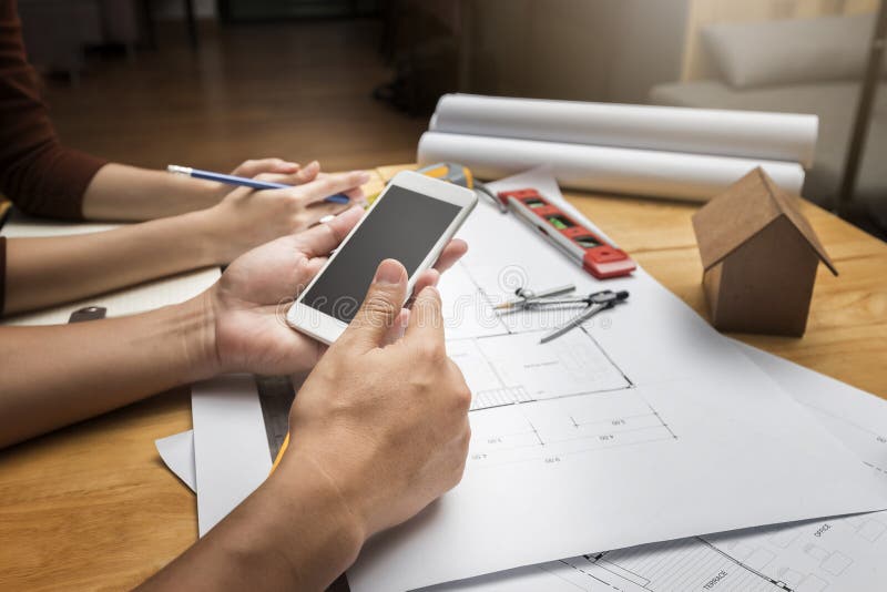 Group of Two Coworkers Using Smartphone and Working with Blueprint in ...
