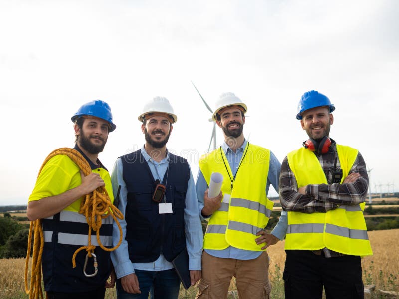 Group of Workers and Engineers in a Field of Windmills Looking at ...