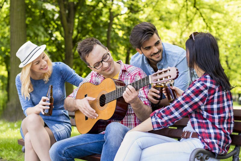 Group of Young Friends Playing Guitar and Drinking Beer on a Park Bench ...