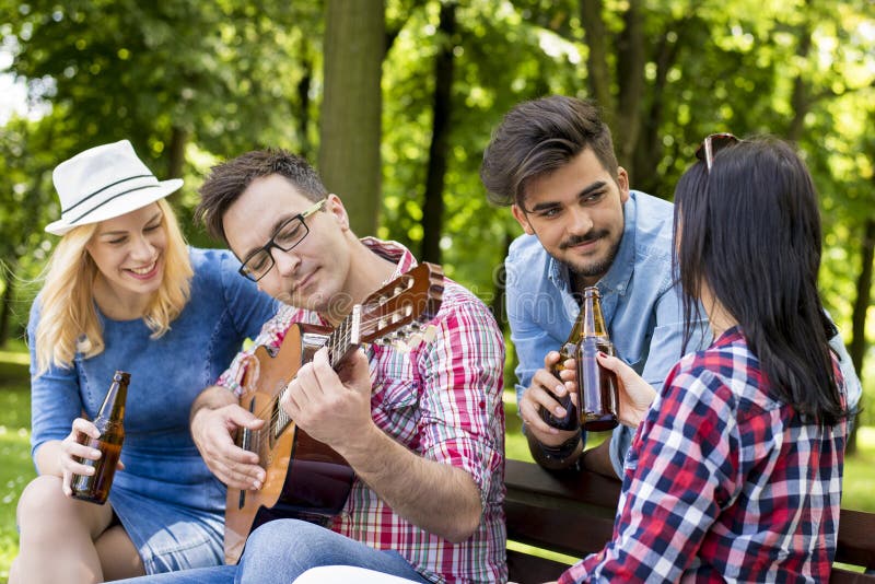 Group of Young Friends Playing Guitar and Drinking Beer on a Park Bench ...