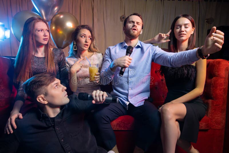 Group Of Young People Singing Into Microphone In Karaoke Bar Stock