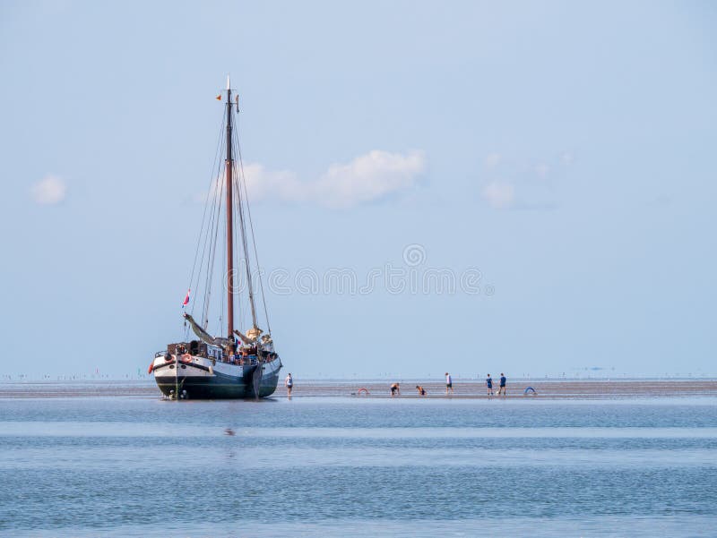 Group of Youngsters on Sand Flat and Flat-bottom Sailboat at Low ...
