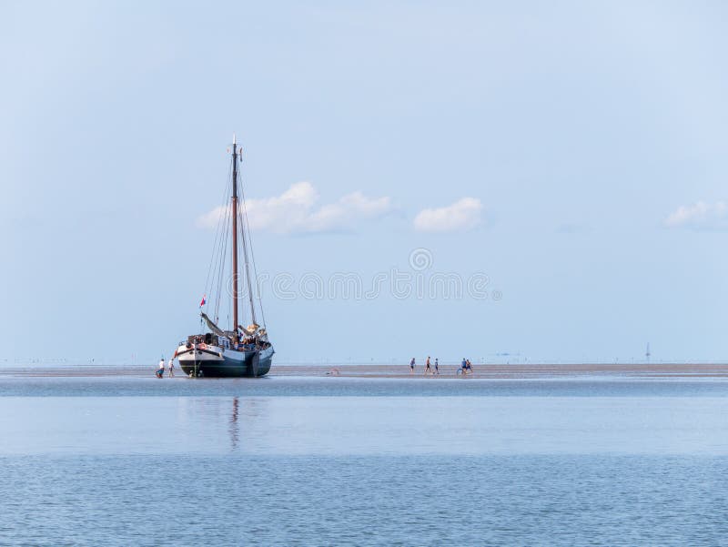 Group of Youngsters on Sand Flat and Flat-bottom Sailboat at Low ...