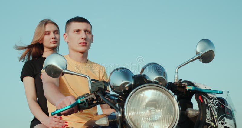 A Guy and a Girl are Sitting on a Motorcycle, Looking into the Distance ...