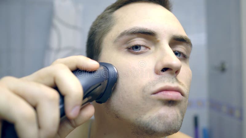 The Guy Shaves with an Electric Razor in the Bathroom. the Guy is ...
