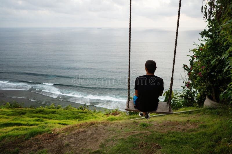 Guy Sits on a Swing on a Cliff by the Ocean at Sunset in Bali Stock ...