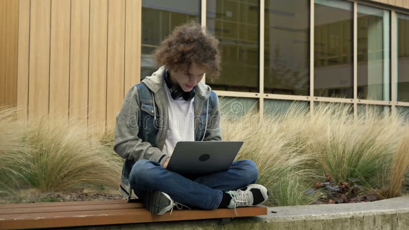 Guy Sitting with a Laptop on a Bench in the Yard of an Educational ...